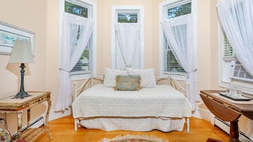 Quarto com cama, mesa de cabeceira, luminária e janela com cortinas.