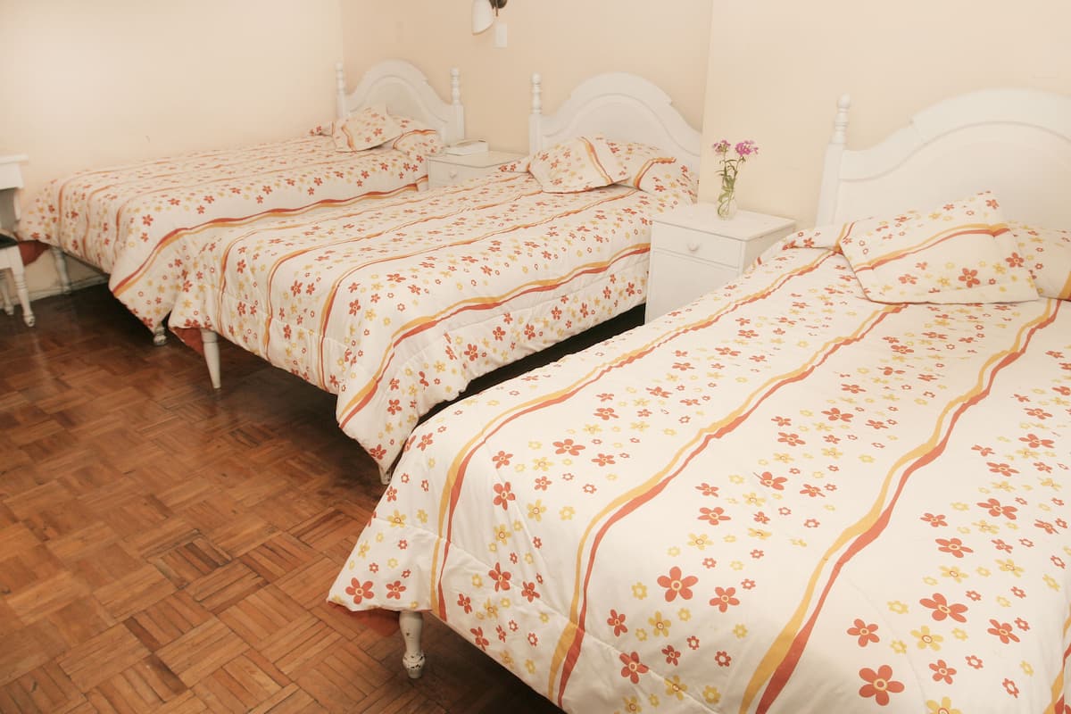 Quarto com duas camas de solteiro, piso de madeira, cabeceiras brancas e uma mesa de cabeceira com um vaso de flores.