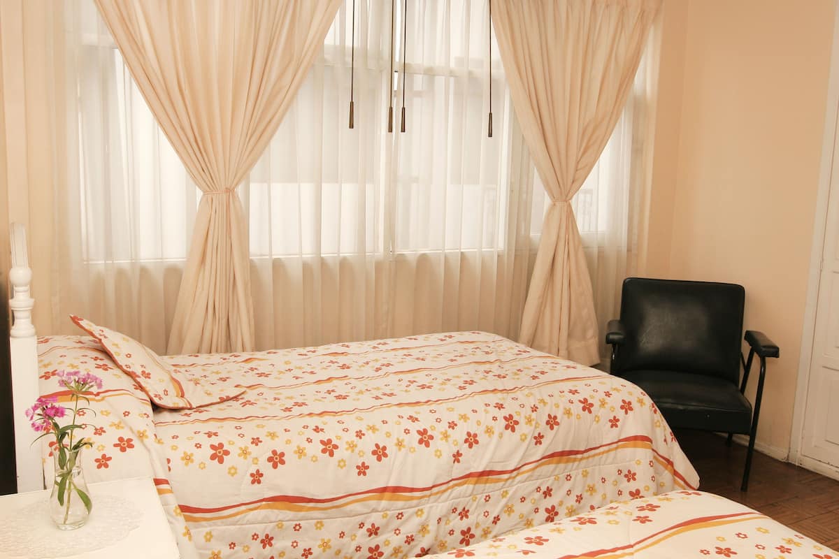 Quarto com uma cama, uma cadeira e um vaso com flores.