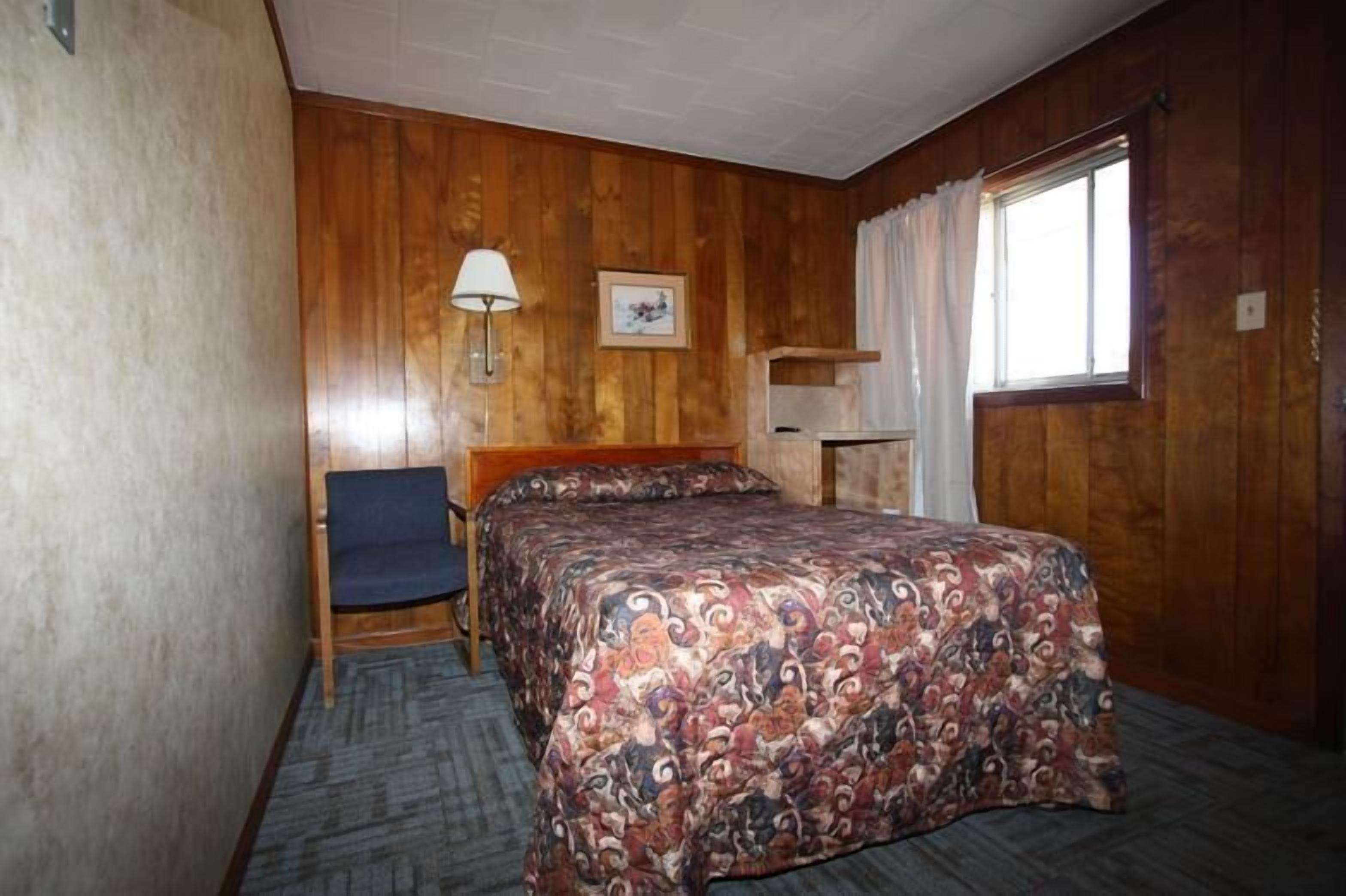 Um quarto com uma cama, uma cadeira, um abajur e uma janela.
