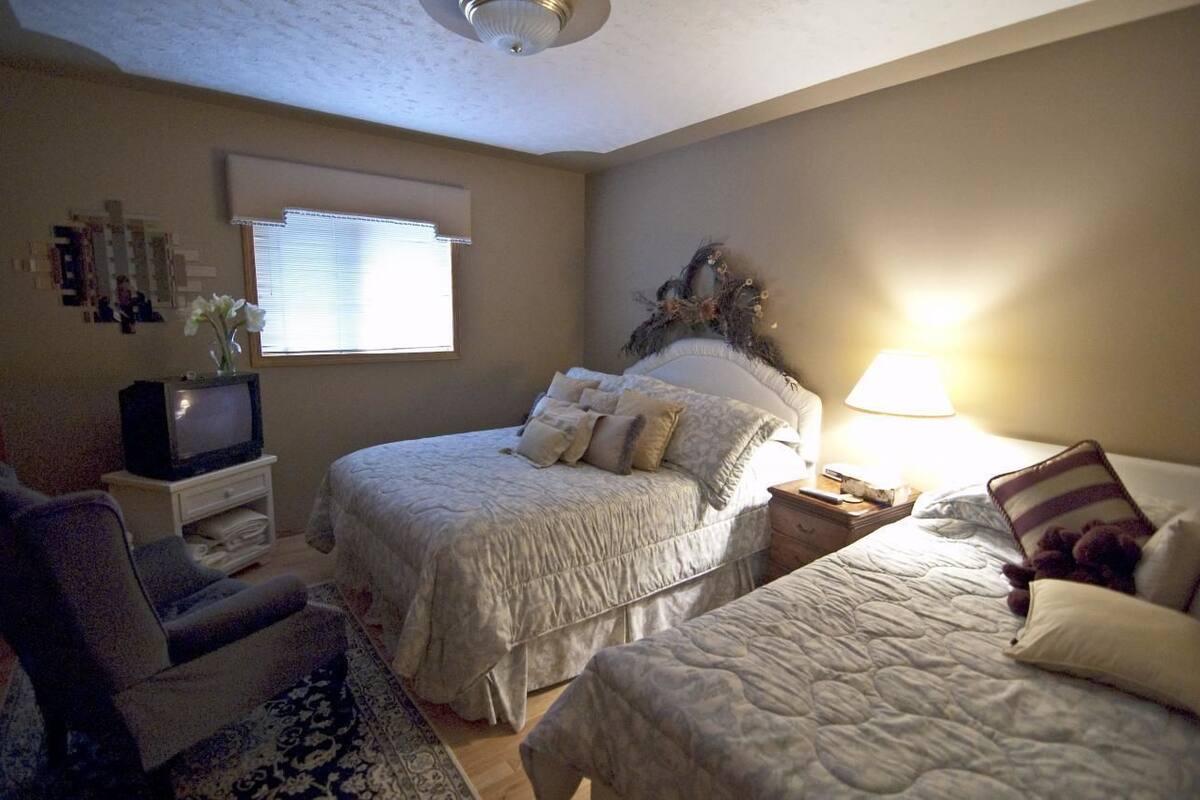 Quarto com duas camas, televisão, abajur e janela com persianas.