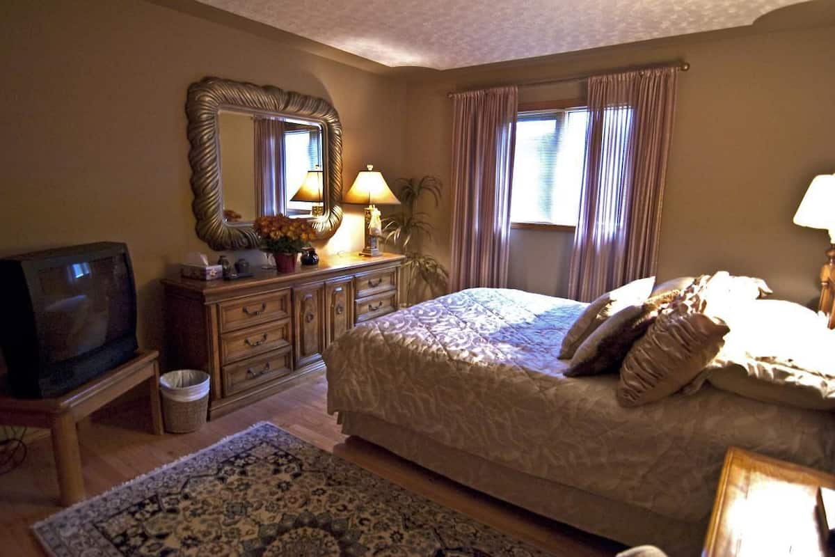 Quarto com uma cama grande, cômoda, televisão e espelho.