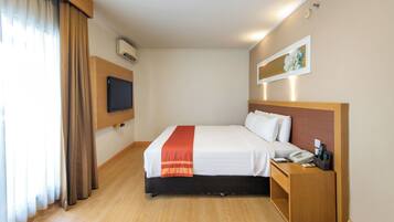 Quarto de hotel com cama, mesa de cabeceira e televisão presa à parede.