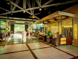 Um hall espaçoso com teto alto, amplas janelas e uma área de recepção com móveis de vime e plantas.