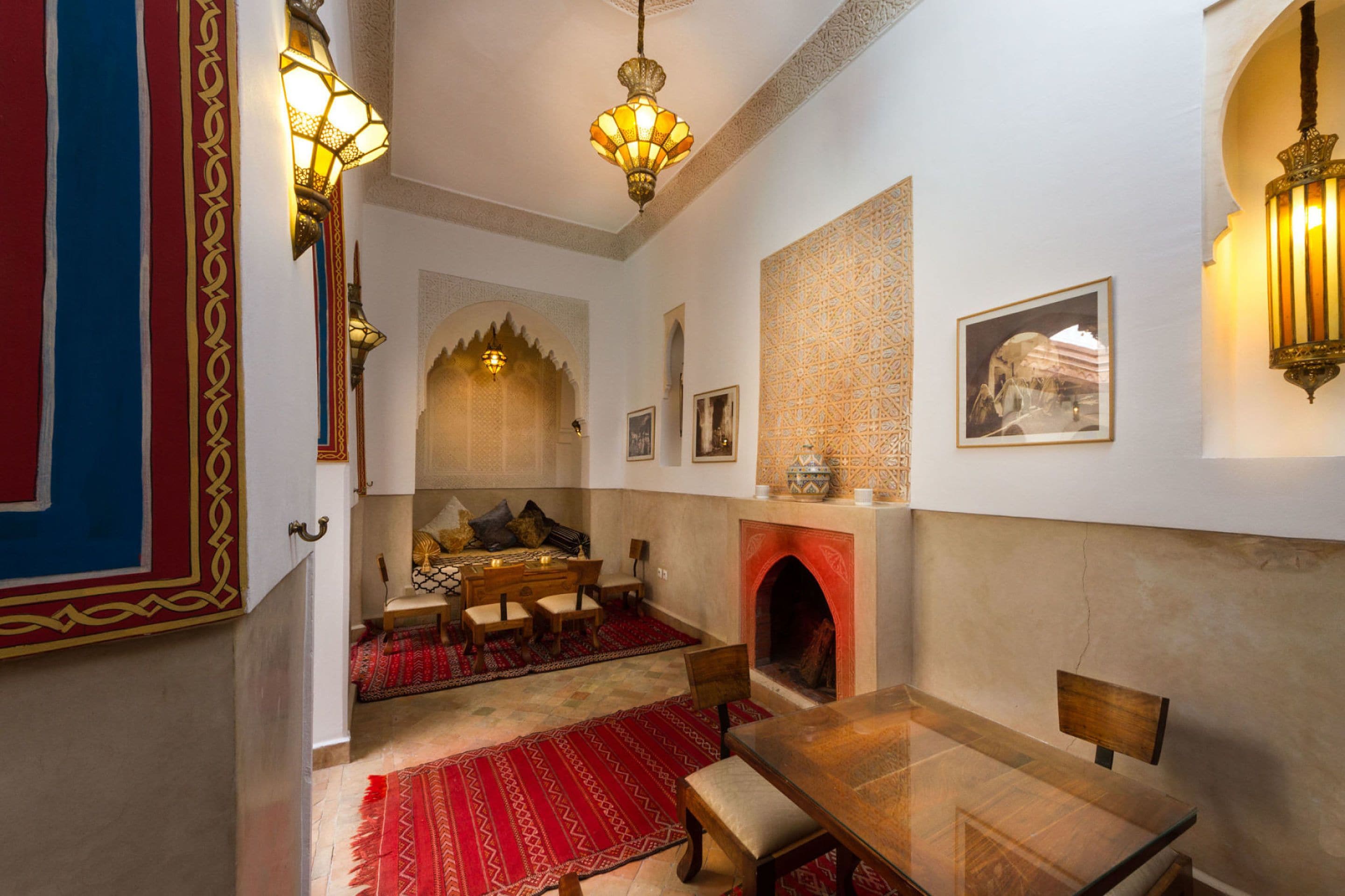 Um interior tradicional marroquino com uma mesa de jantar de madeira, tapetes vermelhos e decorações de parede ornamentadas.