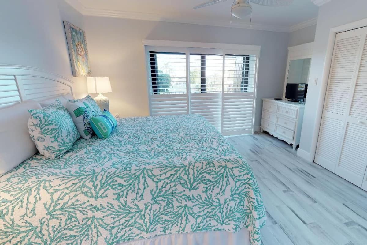 Quarto com cama, mesa de cabeceira, luminária, cômoda, televisão e guarda-roupa.