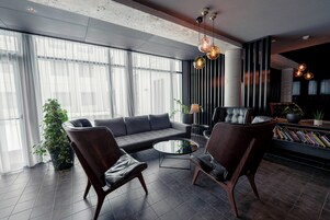 Uma sala de estar moderna com um sofá cinzento, poltronas de couro, uma mesa de centro e uma estante com livros.