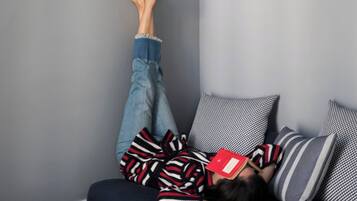 Uma pessoa deitada em uma cama com roupa de cama listrada, um livro vermelho e almofadas estampadas.