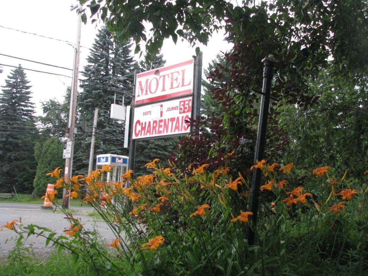 Placa de motel com esquema de cores vermelho e branco, rodeada por vegetação exuberante e flores laranjas.