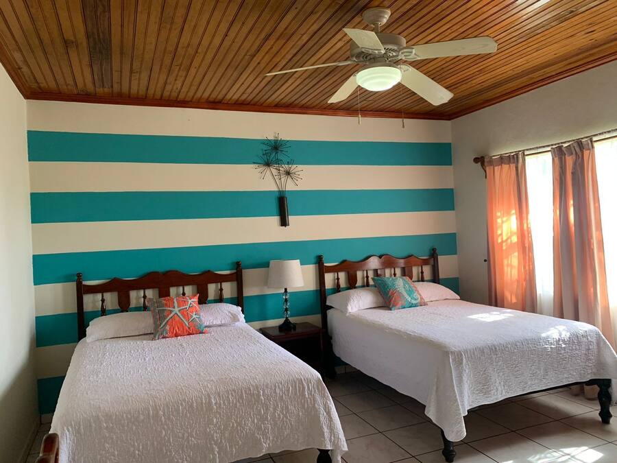 Quarto com duas camas, ventilador de teto e relógio na parede.