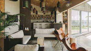 Um interior moderno com teto de madeira, luminárias industriais pendentes, área de bar com banquetas e uma janela grande com vista para o exterior.