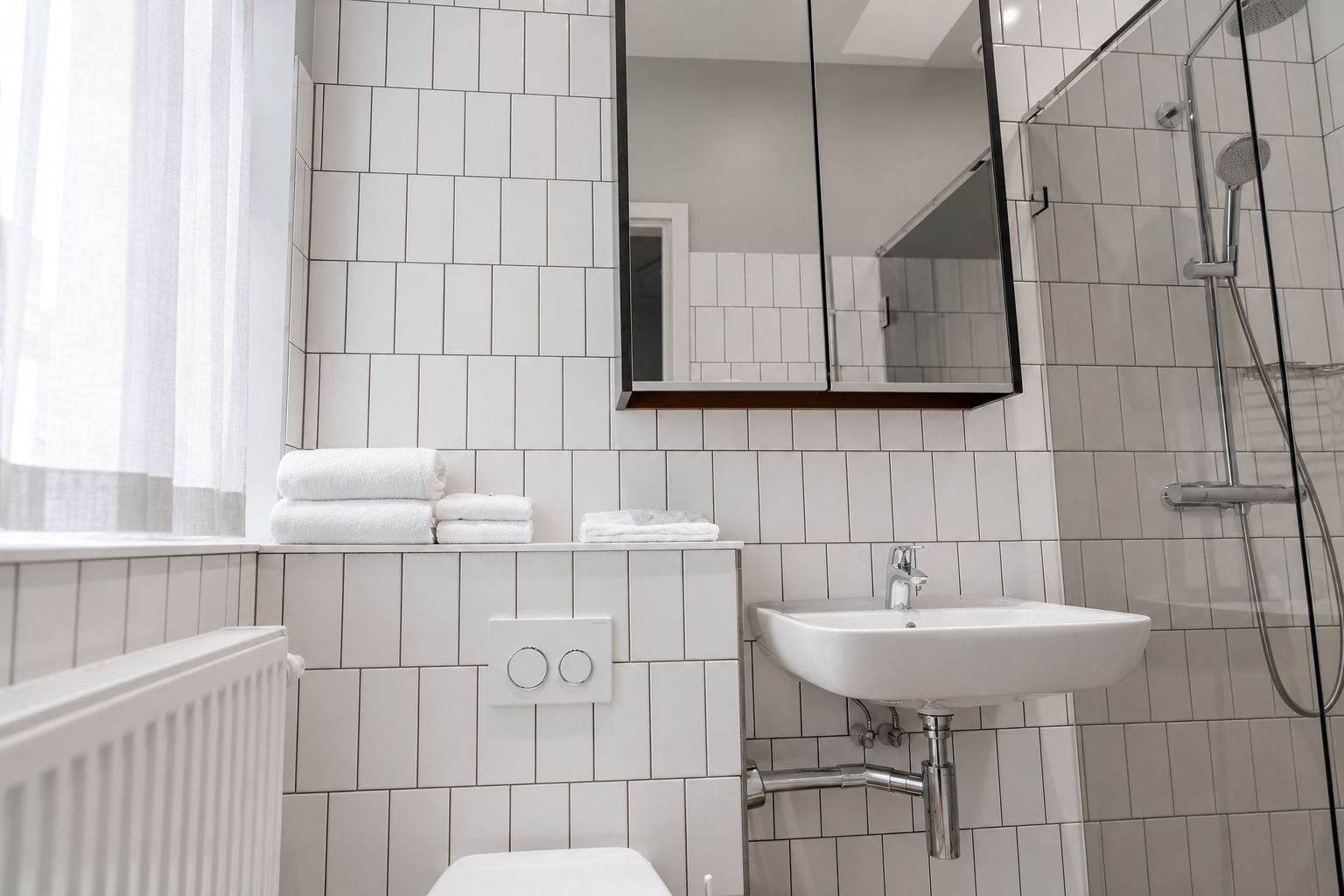 Uma casa de banho moderna com azulejos brancos, uma pia, um espelho e um chuveiro.