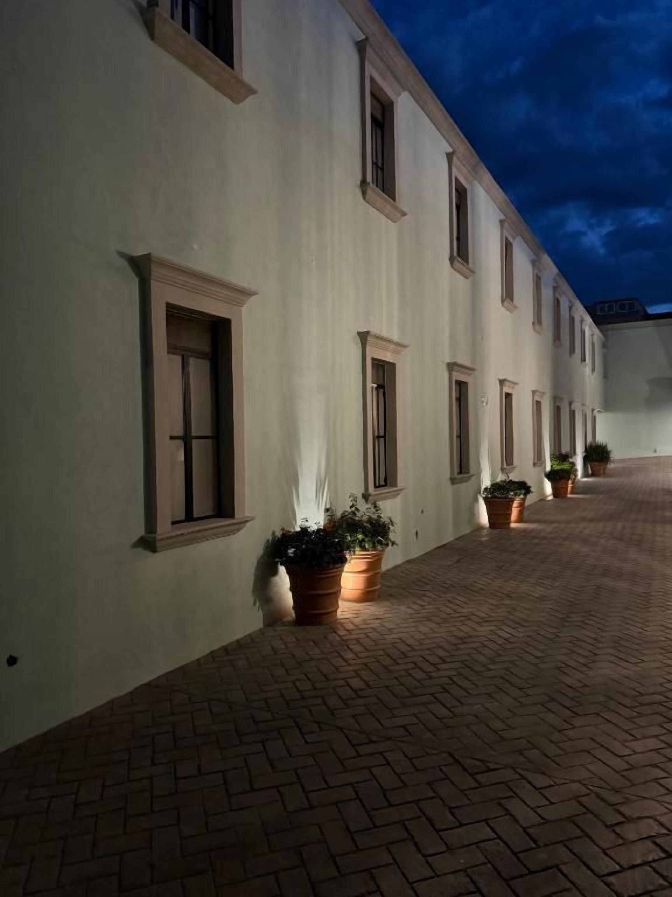Edifício com várias janelas e plantas em vasos ao longo de um caminho de tijolos.