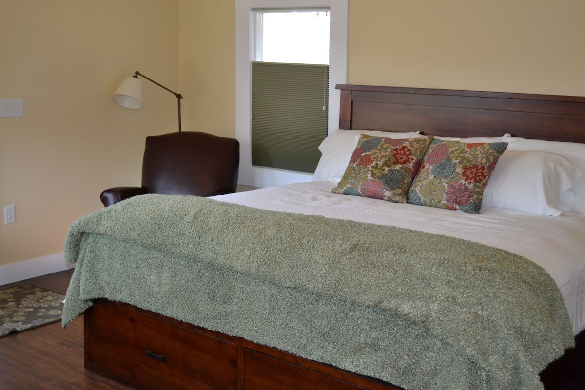 Quarto com cama, cadeira, abajur e janela com persianas.