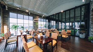 Uma sala de jantar ampla e arejada, com piso de madeira, janelas grandes e cadeiras de vime.