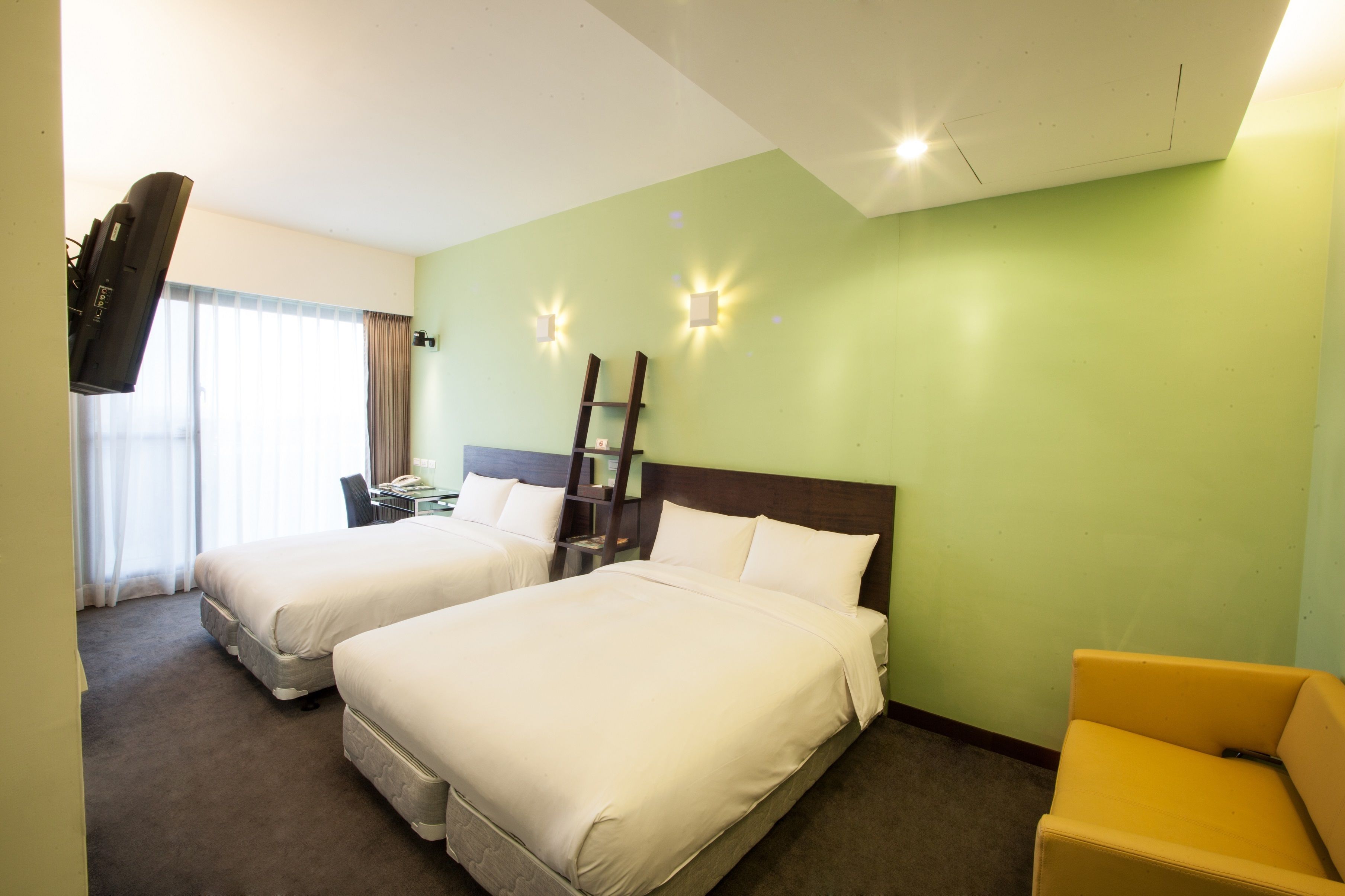 Quarto de hotel com duas camas, uma escrivaninha, uma cadeira e uma TV fixada na parede.