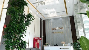 Um saguão de hotel com balcão de recepção, área de estar, janelas amplas e elementos decorativos no teto.