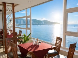 Uma sala de jantar com uma mesa posta para dois, com vista para um corpo de água e um horizonte urbano ao fundo.