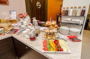 Buffet com diversos alimentos, incluindo frutas, doces e acompanhamentos.