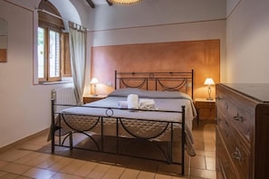 Quarto com cama, duas luminárias laterais, cômoda de madeira e janela com cortinas.