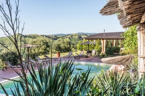 Área de piscina com espreguiçadeiras, um pérgola e vista para colinas ondulantes.