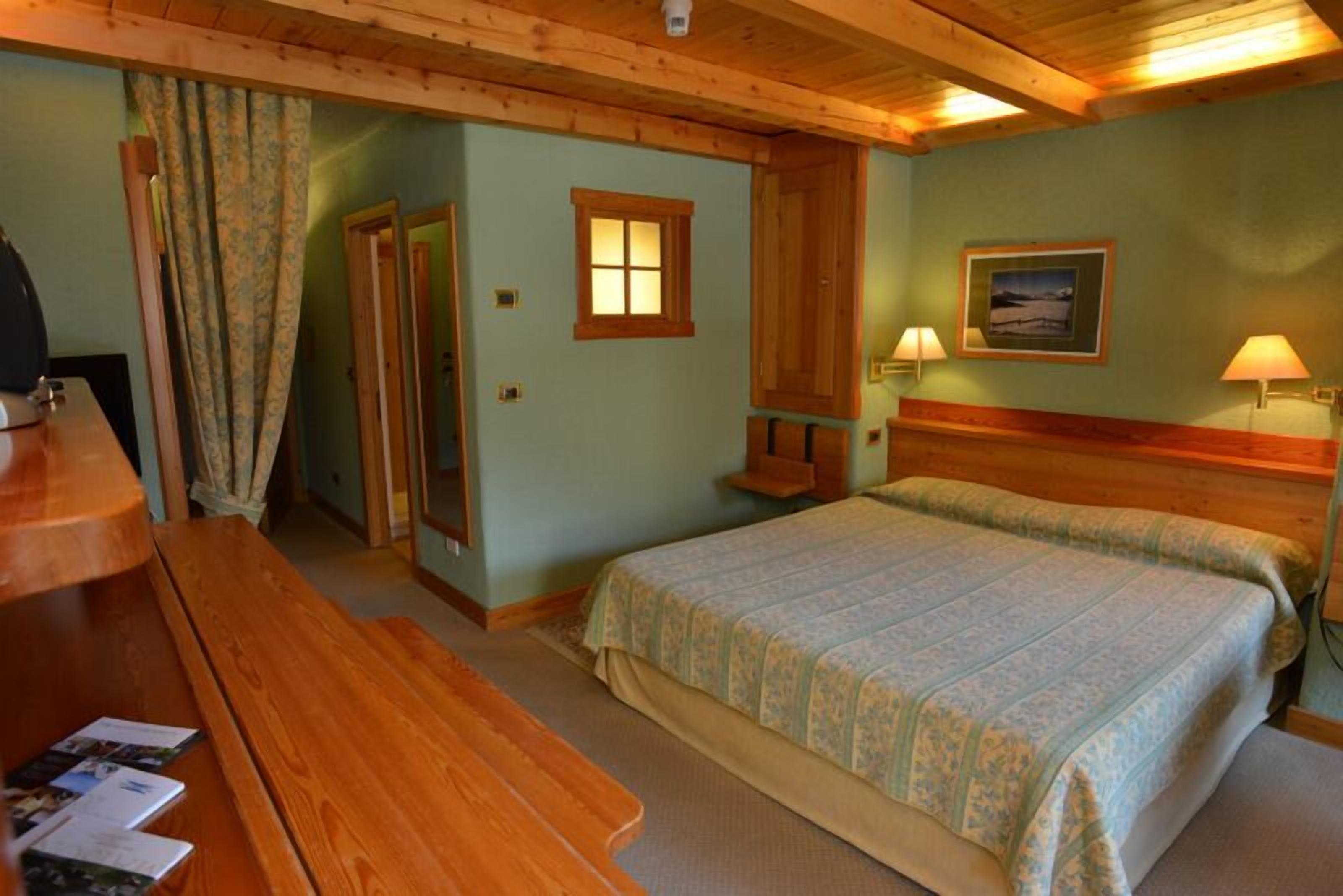 Quarto com cama, um banco de madeira, escrivaninha e mesa de cabeceira.