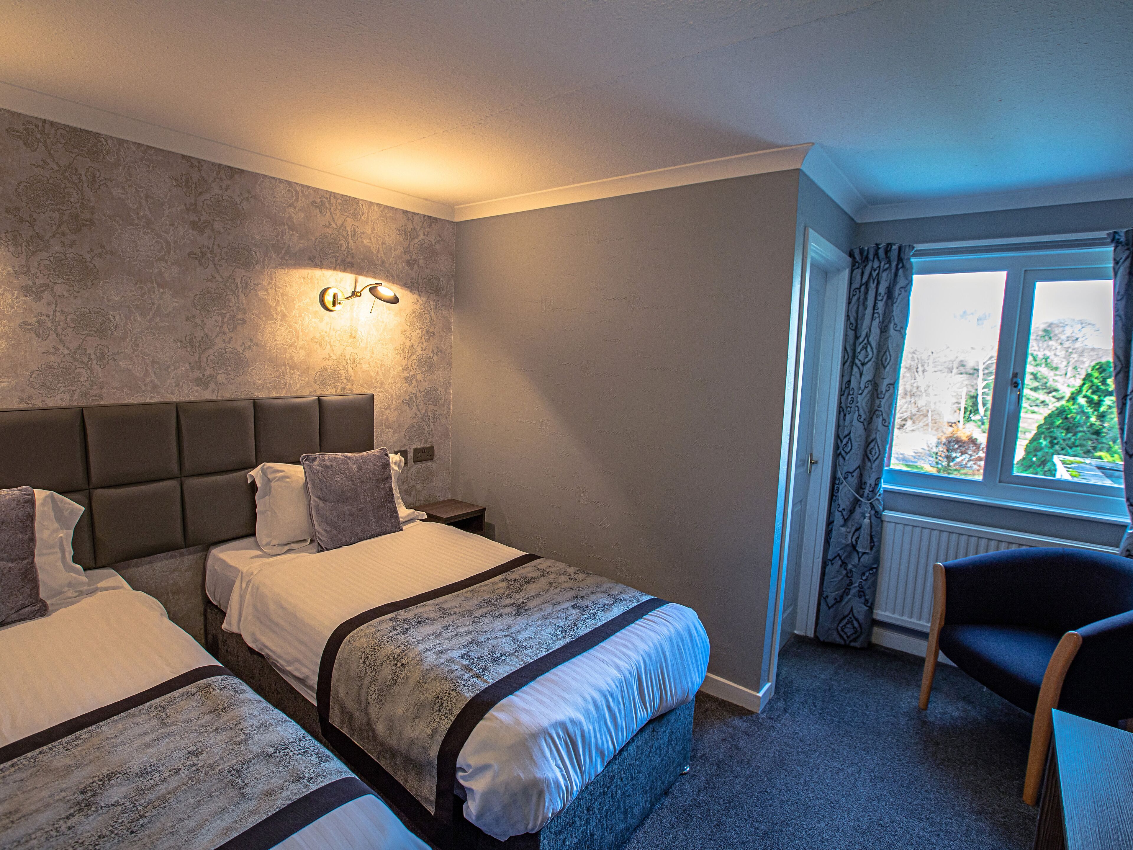 Quarto de hotel com duas camas, uma janela com cortinas e uma cadeira.