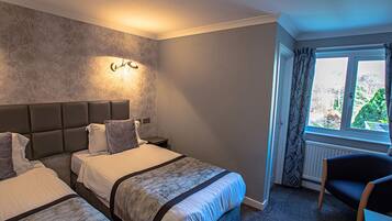 Quarto de hotel com duas camas, uma janela com cortinas e uma cadeira.