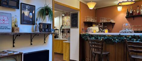 Uma área de bar com balcão, banquetas e diversos copos. Há objetos decorativos na parede, incluindo quadros e uma placa.