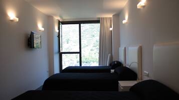 Quarto de hotel com duas camas, uma janela grande com cortinas e luminárias fixadas na parede.