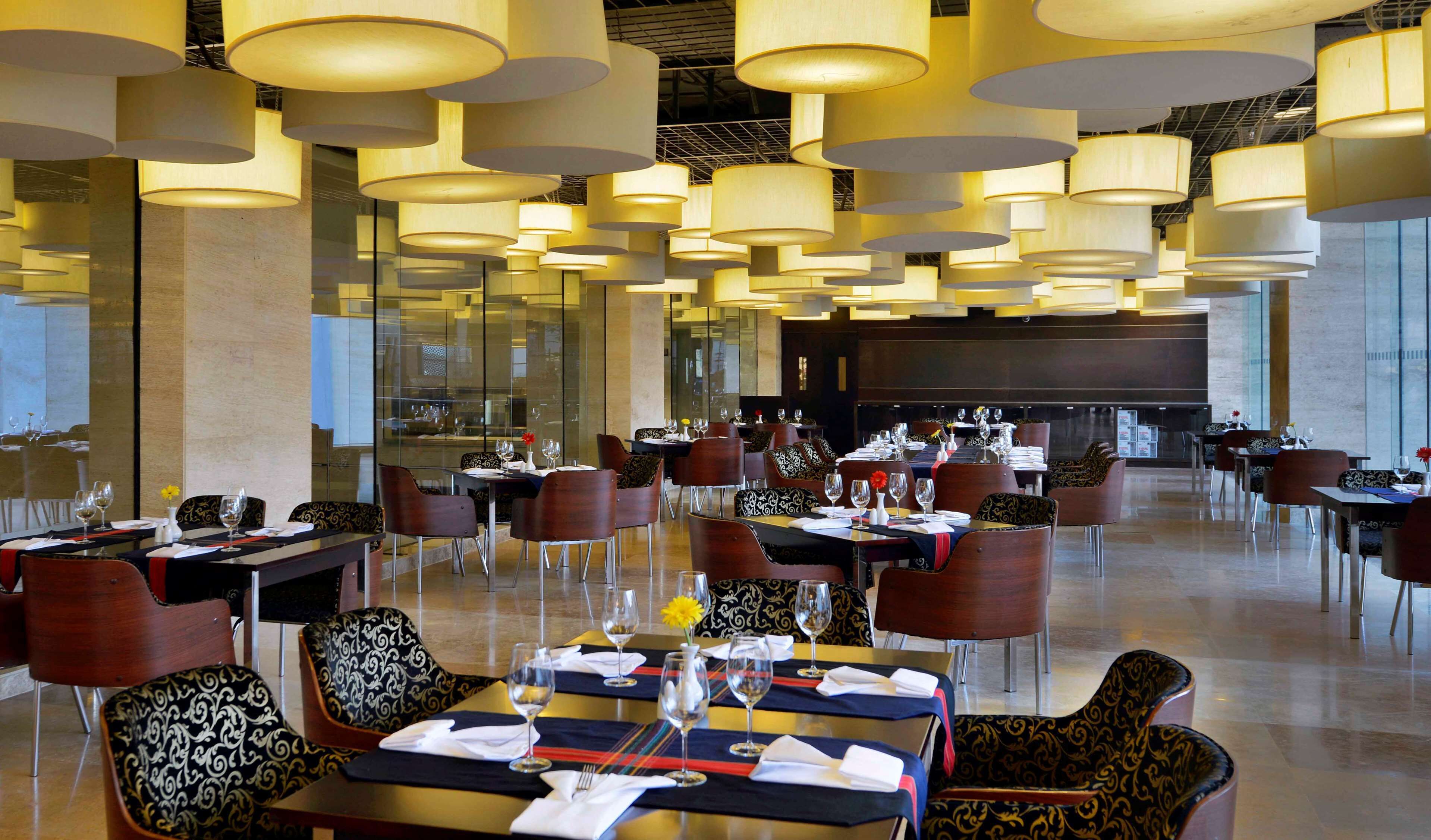 Uma sala de jantar ampla, com várias mesas e cadeiras, luminárias grandes no teto e design de interiores moderno.