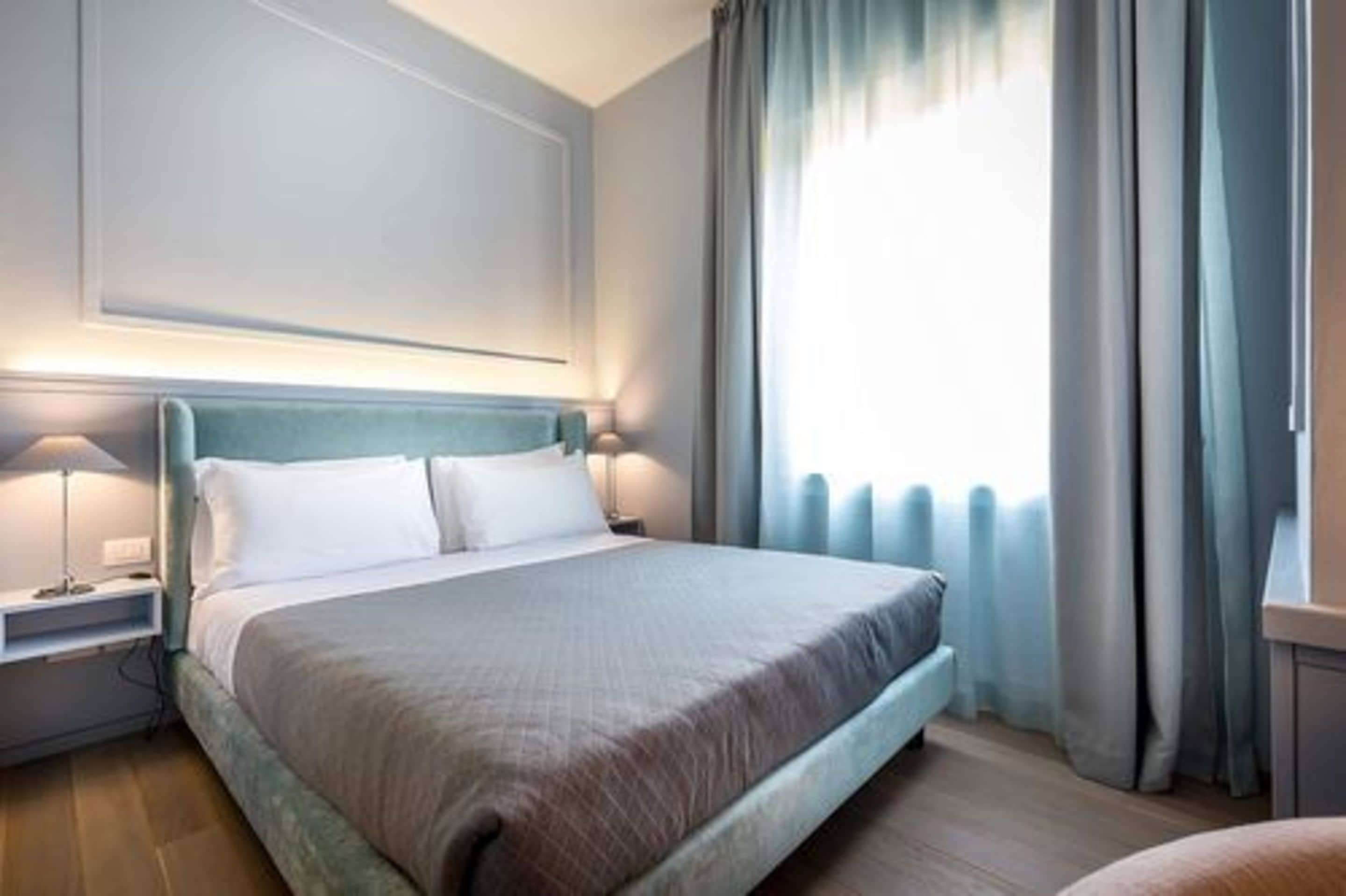 Quarto de hotel com uma cama grande, mesas de cabeceira e uma janela com cortinas.