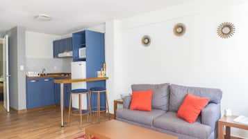 Um espaço de estar compacto com cozinha compacta, um sofá cinza com almofadas vermelhas e uma mesa de centro de madeira.