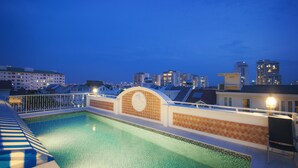 Piscina no terraço com deck revestido, rodeada por edifícios e horizonte urbano ao entardecer.