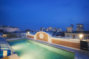 Piscina no terraço com deck revestido, rodeada por edifícios e horizonte urbano ao entardecer.