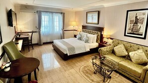 Quarto de hotel com uma cama, uma poltrona verde, um sofá, uma mesa de jantar e uma mesa de centro.