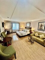 Quarto de hotel com uma cama, uma poltrona verde, um sofá, uma mesa de jantar e uma mesa de centro.