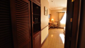 Um corredor de hotel com um guarda-roupa de madeira, uma escrivaninha com abajur e uma cama com cortinas.