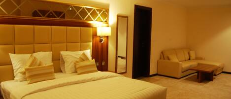 Quarto de hotel com uma cama grande, um sofá, uma mesinha e um espelho.