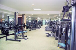 Uma academia com diversos equipamentos de exercícios, espelhos e piso coberto por carpete.