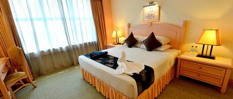 Quarto de hotel com uma cama grande, duas luminárias de cabeceira, uma cadeira, mesa de cabeceira com luminária e janela com cortinas.