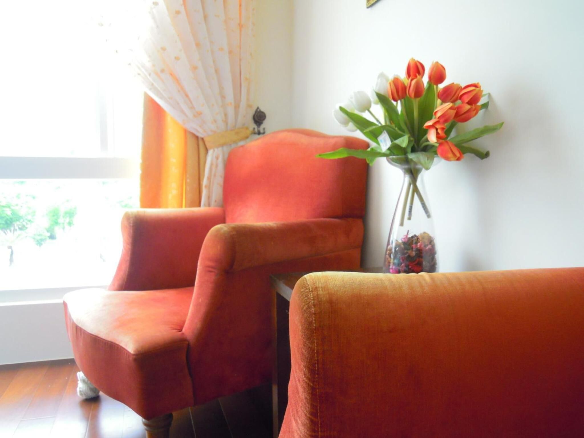 Um quarto com duas poltronas vermelhas e um vaso de tulipas laranjas sobre uma mesa.