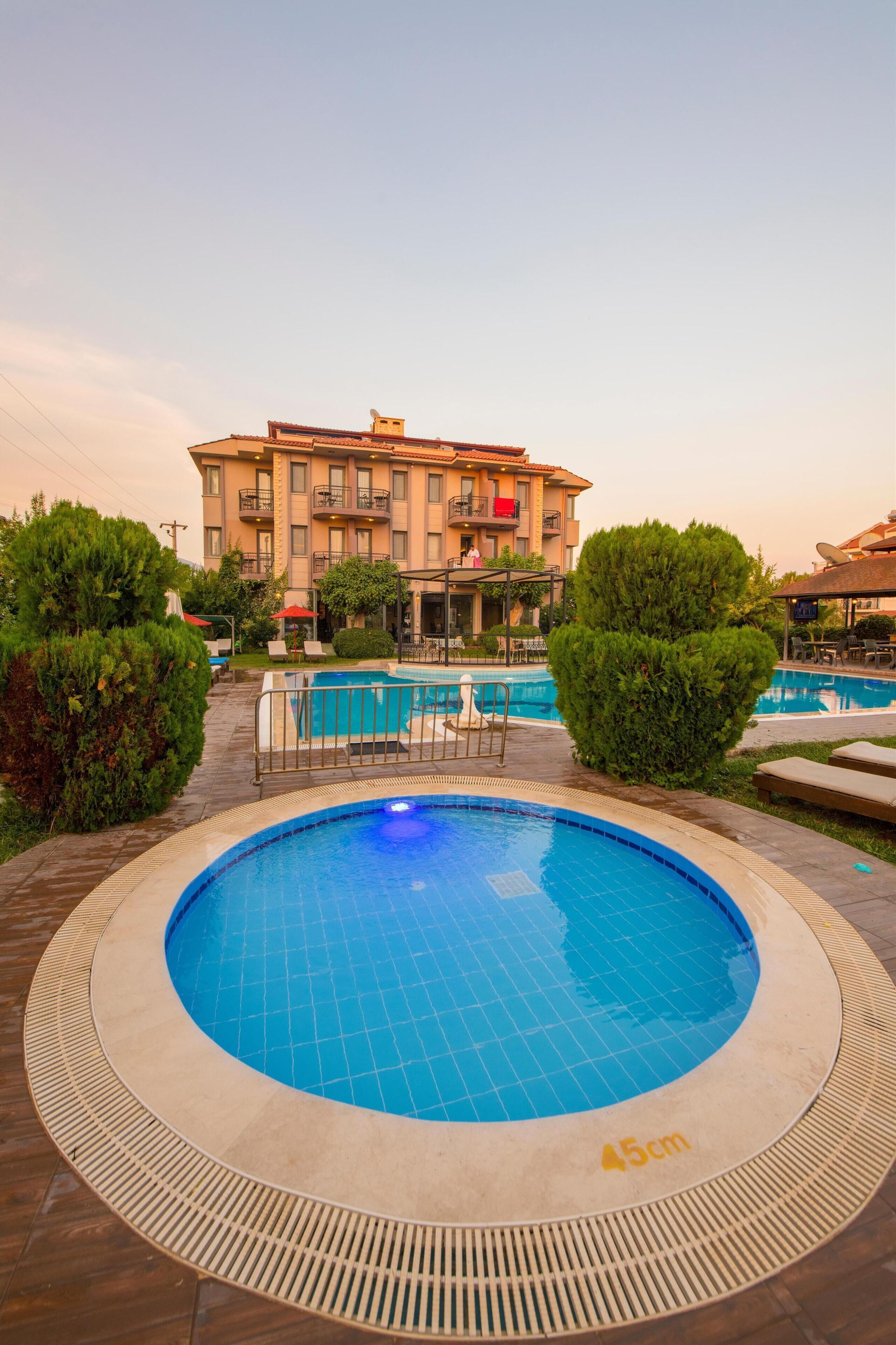 Uma piscina com indicador de profundidade de 45 centímetros, rodeada por um deck ladrilhado e um edifício com varandas ao fundo.
