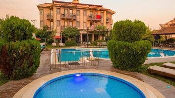 Uma piscina com indicador de profundidade de 45 centímetros, rodeada por um deck ladrilhado e um edifício com varandas ao fundo.