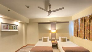 Quarto de hotel com duas camas de solteiro, um ventilador de teto, uma mesinha com um telefone e uma luminária na parede.
