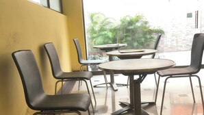 Uma área de refeições com uma mesa redonda e quatro cadeiras, piso ladrilhado e vista para o verde lá fora.