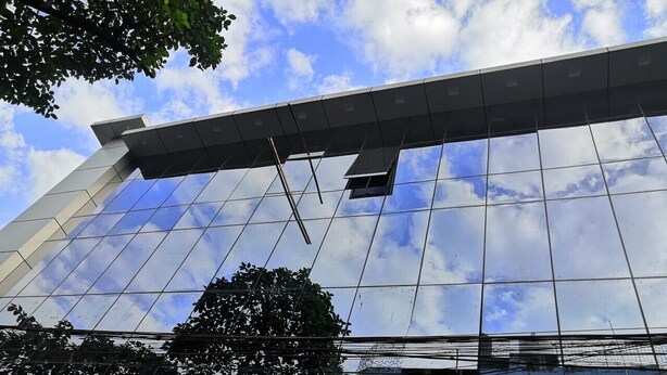 Um edifício moderno com fachada de vidro refletindo o céu e as nuvens.
