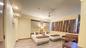 Quarto de hotel com duas camas, um sofá, uma mesa e uma janela grande com cortinas.