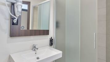 Casa de banho com lavatório branco, espelho, secador de cabelo e porta-toalhas.
