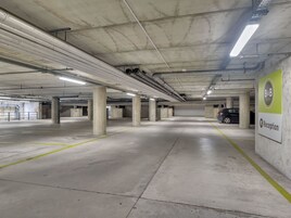 Amplo espaço de estacionamento subterrâneo, com pilares de concreto, iluminação fluorescente e placa de recepção.